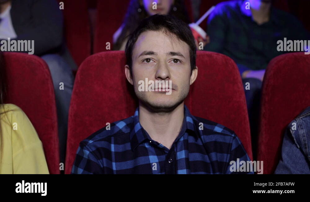 A young emotional guy watches a sad movie in a movie theater and cries ...