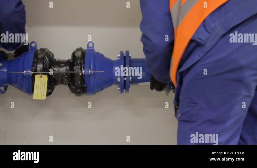 Two workers connect a hydraulic pipe connector between two pipes ...