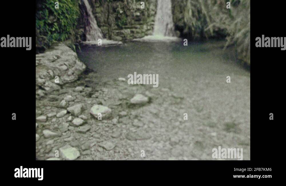 1970s: Tilt up pond to waterfalls. Low angle pan from grass to rock ...