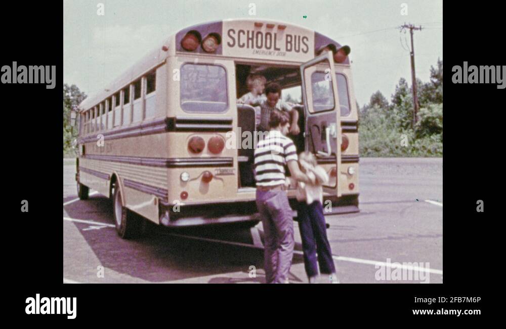 1970s: Man helps children exit bus through rear door. Driver exits bus ...