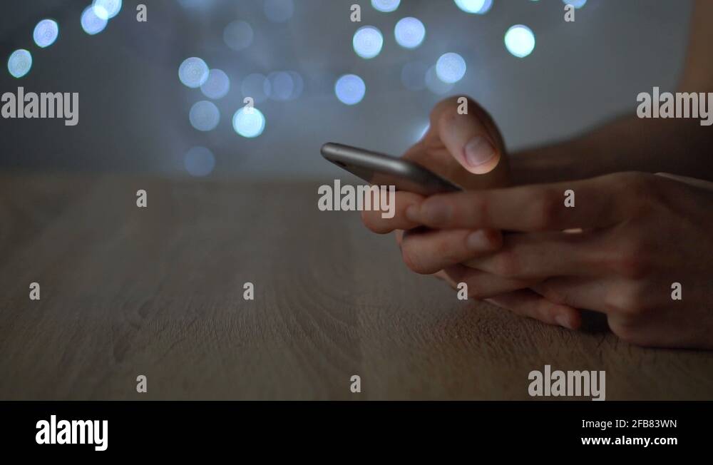 Man scrolling on his phone on a wooden table, with lights in the background Stock Video Footage ...