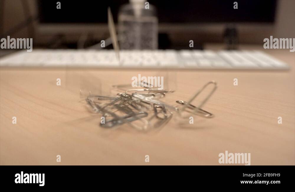 A hand full of paper clips slowly dropping onto an office desk in super ...