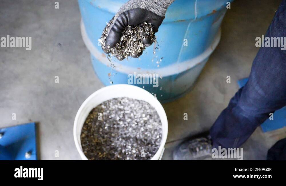 Moving shot of gloved hand dropping processed metal scrap into a bucket ...