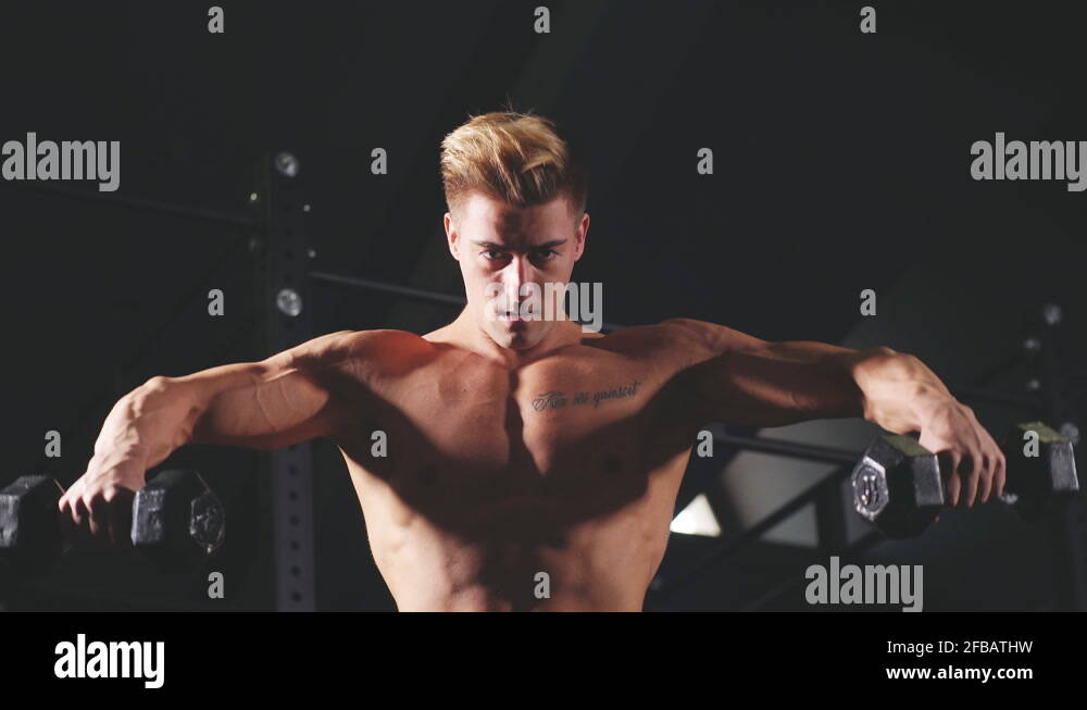 Shirtless white man starting exercise with dumbbell weight in dark gym ...