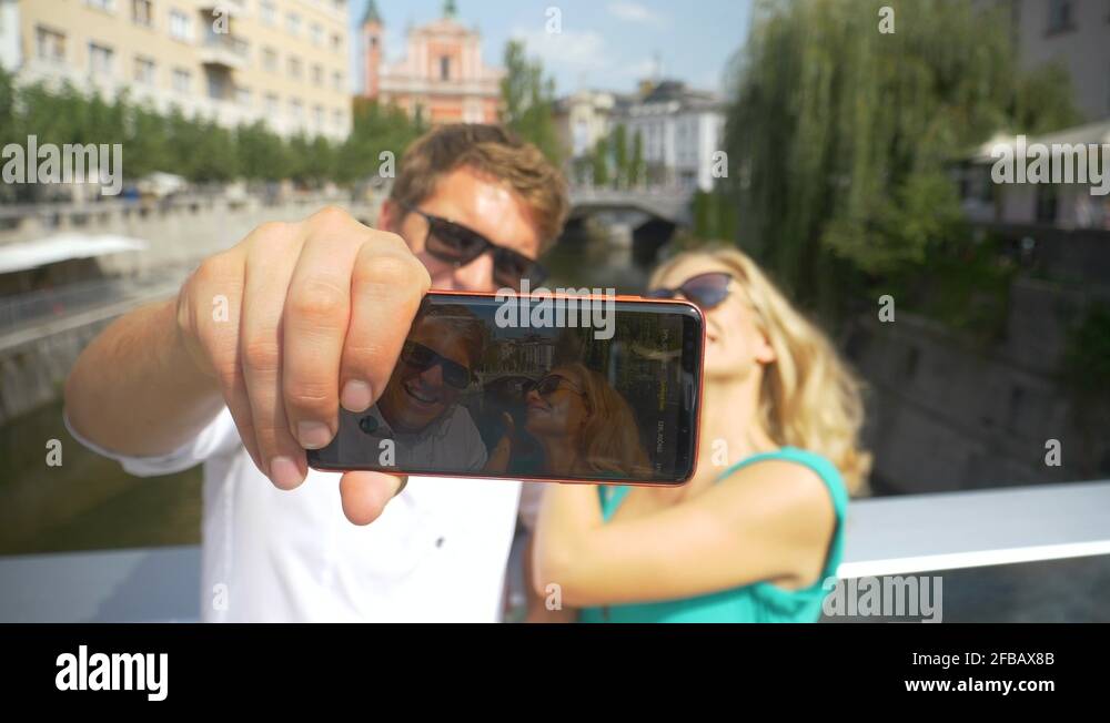 CLOSE UP: Tourist couple making goofy faces while taking selfies from a ...