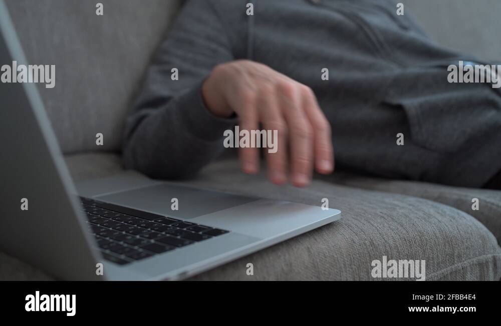 Tired guy typing slowly on his computer while sitting on couch Stock ...
