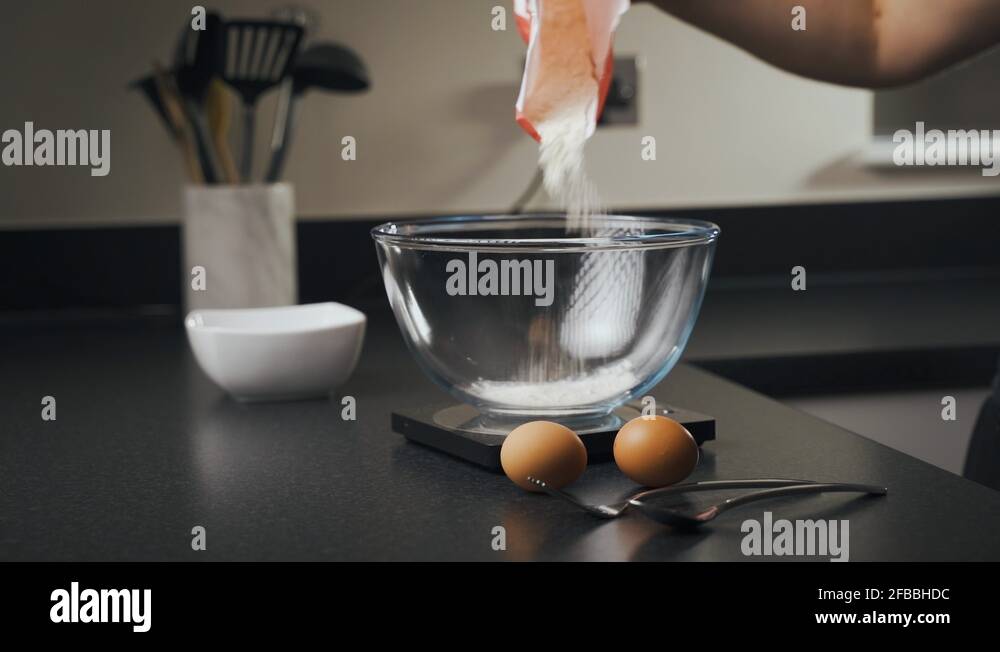 Man shaking flour into a clear glass bowl and weighing the ingredients ...