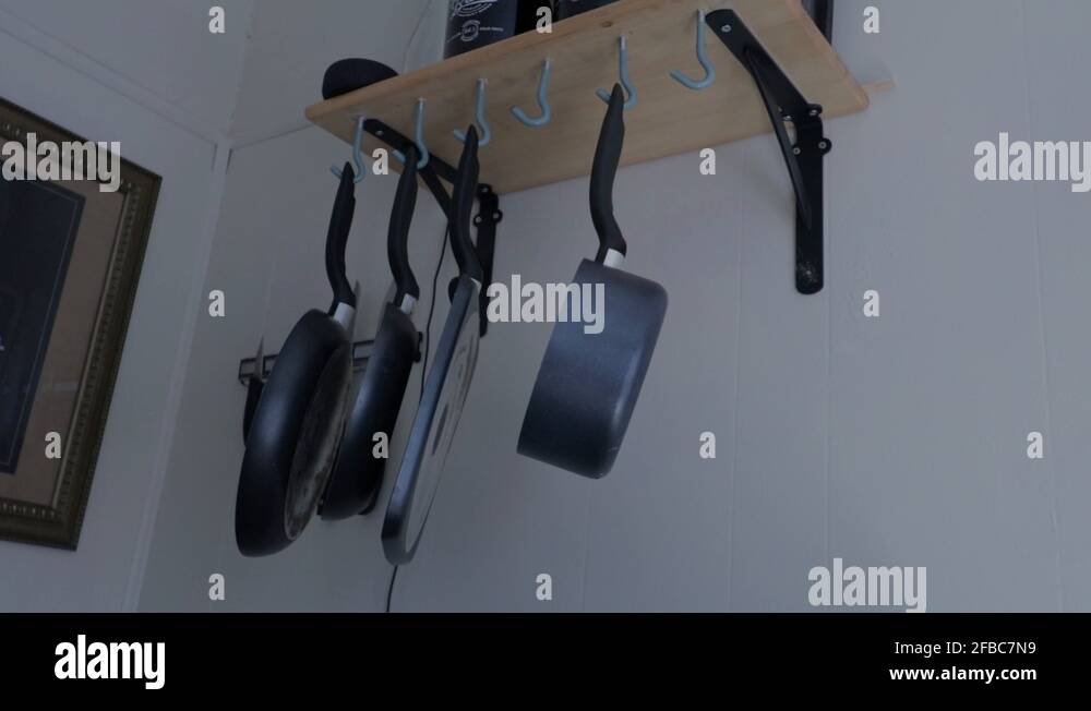 Pans hanging above a stove. Man hangs a cast iron skillet next to the ...
