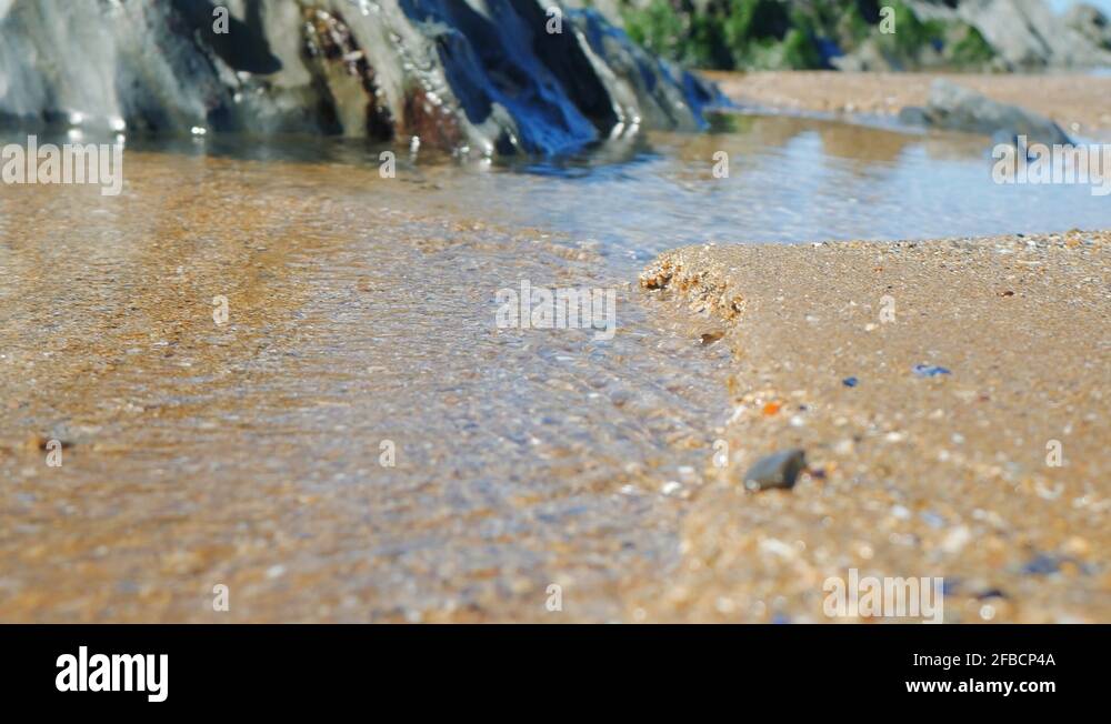 Slow pan from left to right showing a clear flowing stream on a beach ...