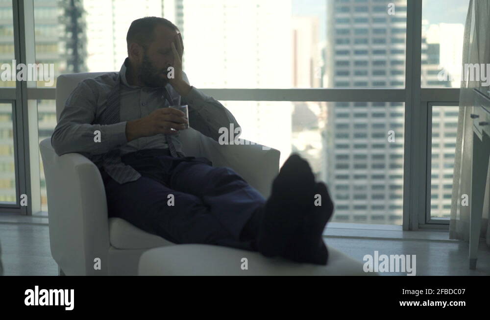 Drunk businessman drinking alcohol sitting on chair at luxury home ...