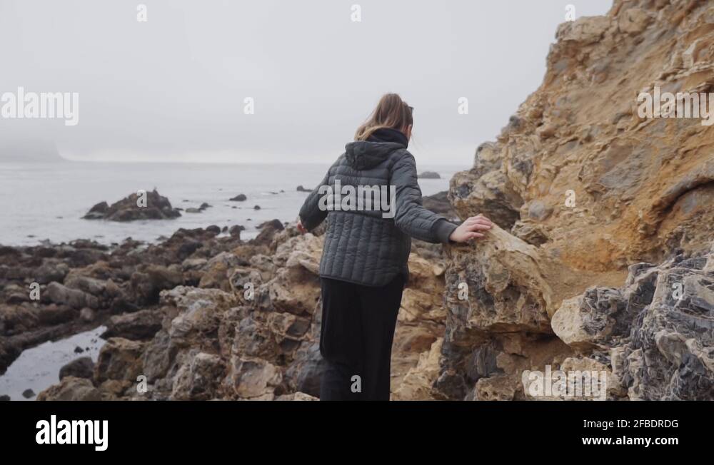 girl climbing the rocks forward and looking back at the camera against ...