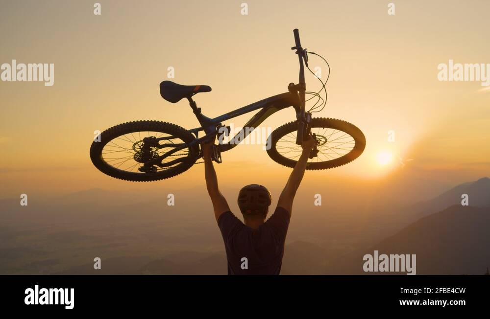 LENS FLARE: Excited man lifts his bike above his head after a fun bike ...