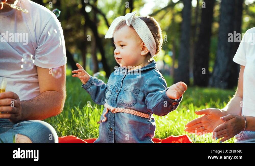 baby girl catching soap bubbles blown by her father at family picnic in ...