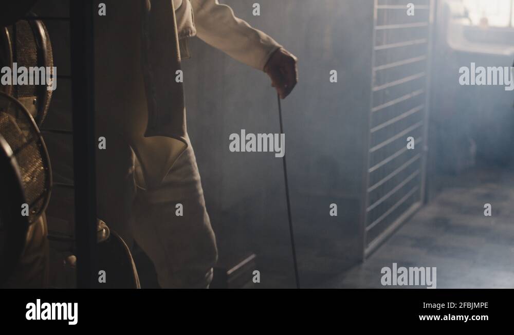 Man in a fencing uniform stands in a locker room checking out his gear ...