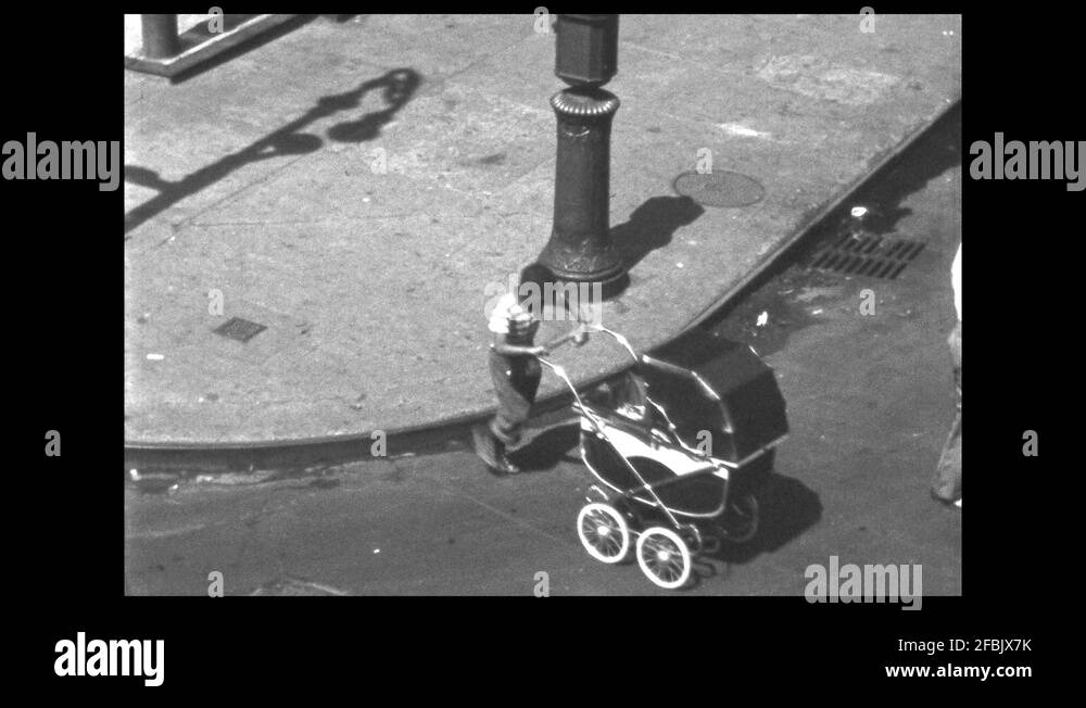 1940s: City street. Boy pushes baby carriage through crosswalk and onto ...