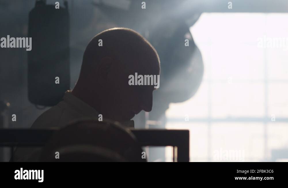 A male fencer adjusting his fencing mask in a dark gym locker room ...