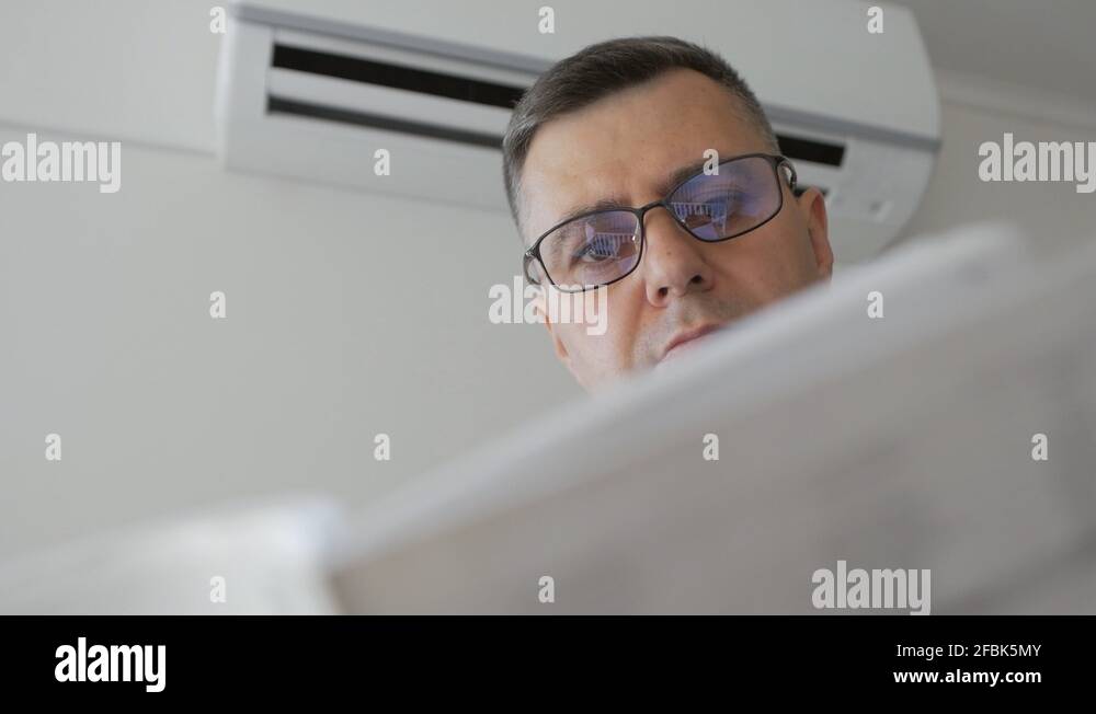 A man with glasses standing next to a working air conditioner is ...