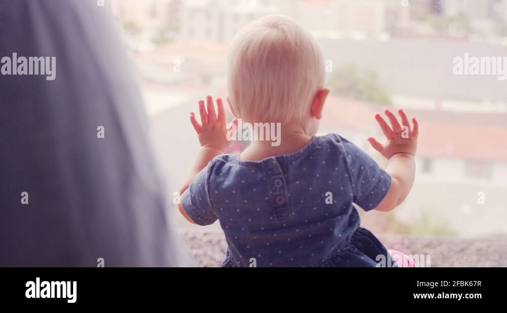 Young curious baby girl looking out glass window of apartment building ...