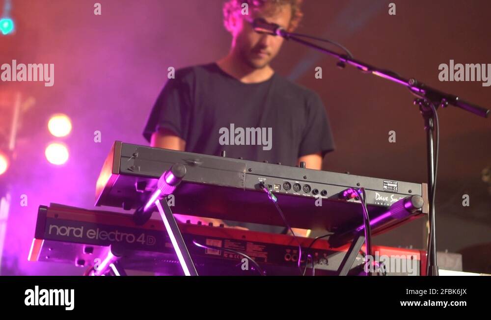 A young happy male keyboard player smiles at the band while being lit ...