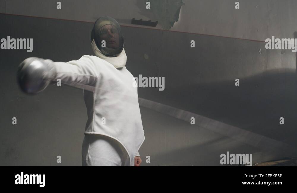 Man with his fencing foil pointing at the camera, pulls off his fencing ...