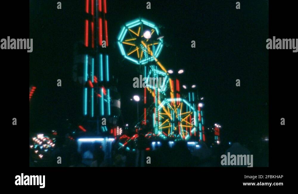 1950s: Neon lights at carnival during night. Amusement rides spin and ...
