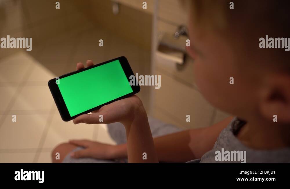 smartphone with green screen in hand of little kid sitting in toilet 4k ...