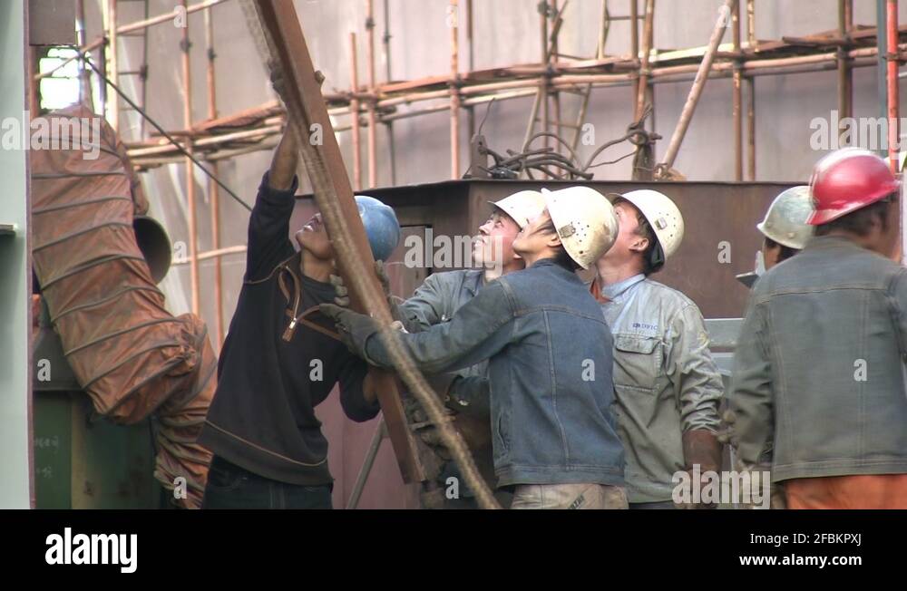 Chinese workers with safety helmets lift heavy materials at shipyard ...