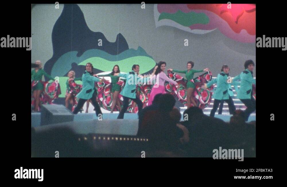 1970s: Men and women dance and sing on stage. Broadcast cameras point ...