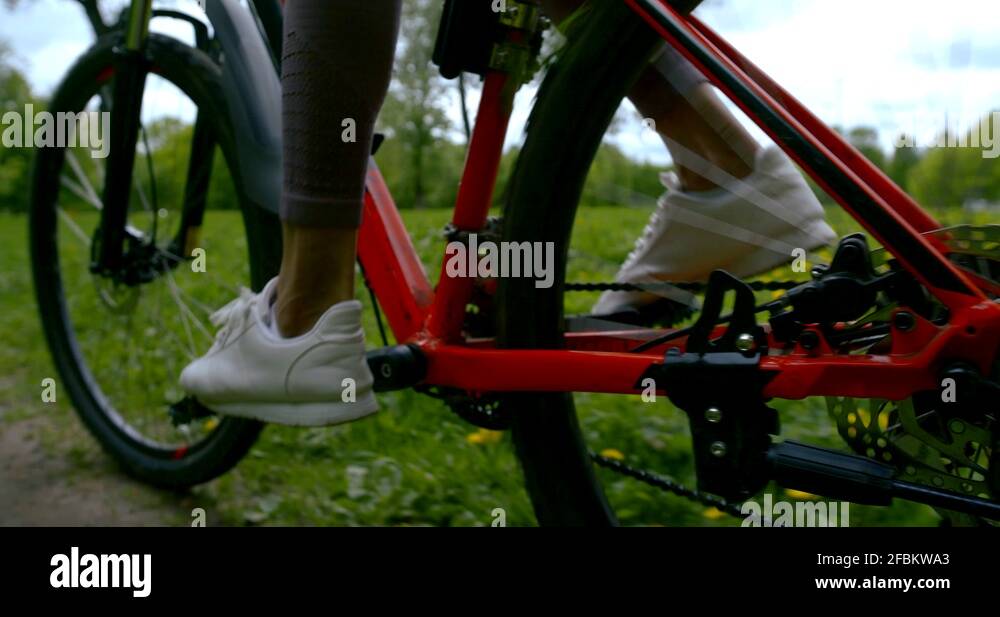Legs girls close-up ride on a red bike on the path past the field with ...