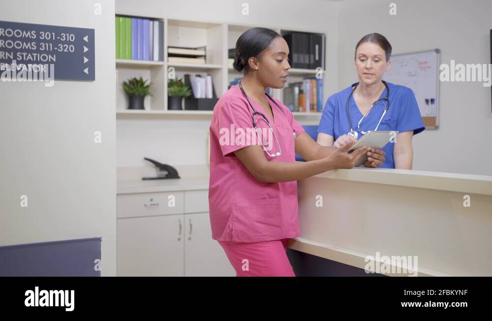 Two nurses w/ stethoscopes at nurses station review chart, camera move ...