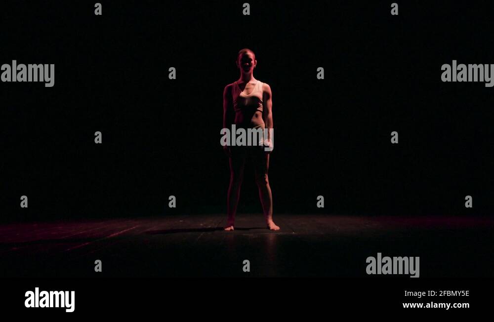 Female contortionist circus performer performing routine in dark studio ...