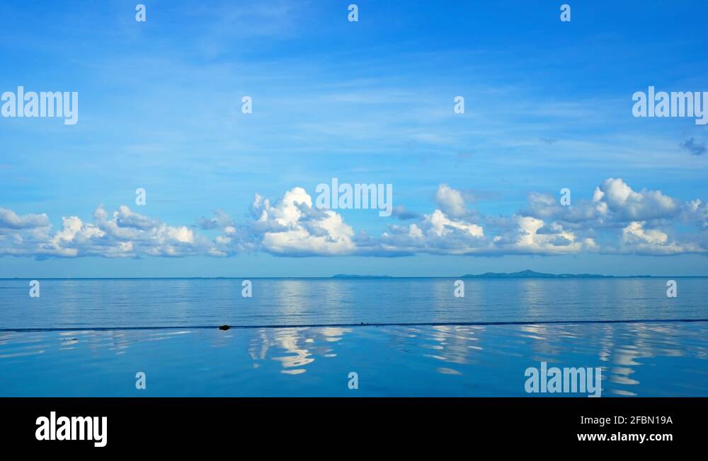 Static shot of an infinity pool with the ocean behind it and blue skies ...