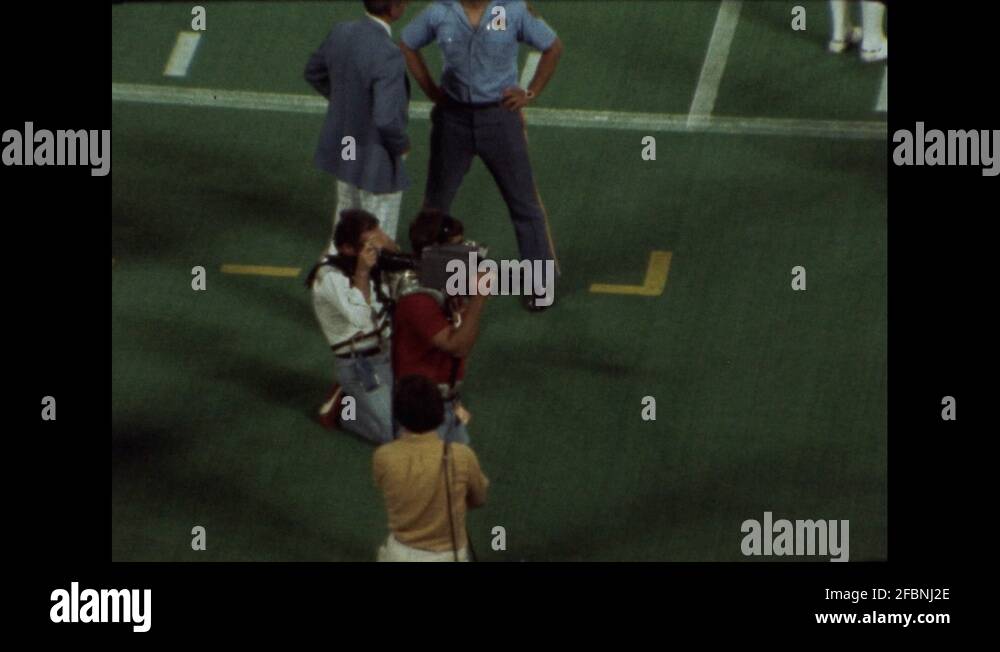 1970s: Camera people point cameras at football field. Cameraman walks ...