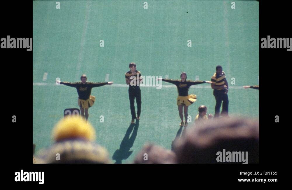 1970s: Football field. Cheerleaders in yellow & black cheer on the ...