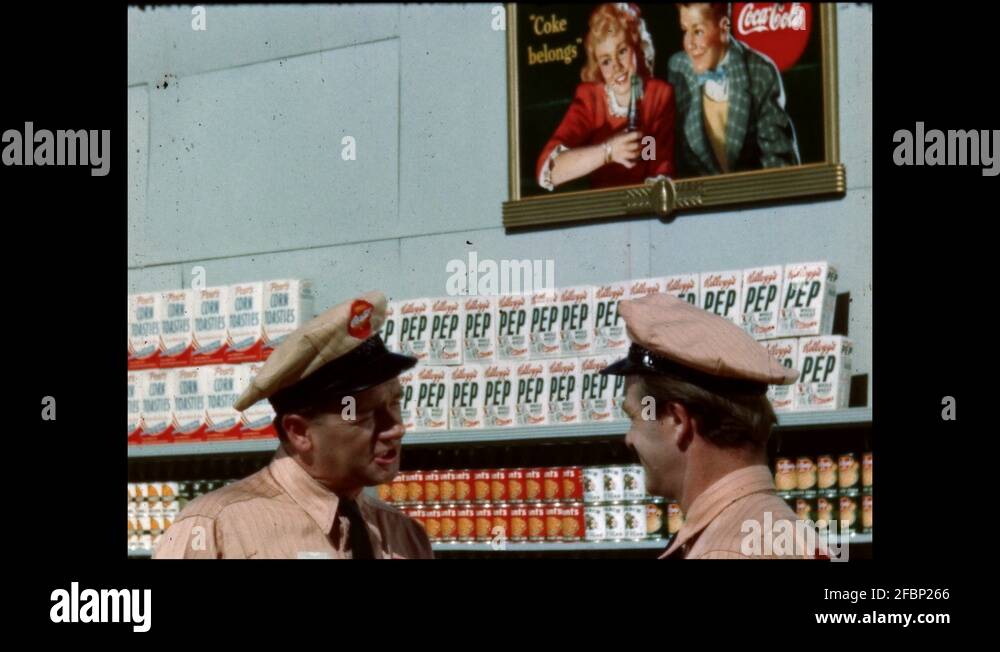 1950s: Two Coca-Cola deliverymen talk in a grocery store under a poster ...