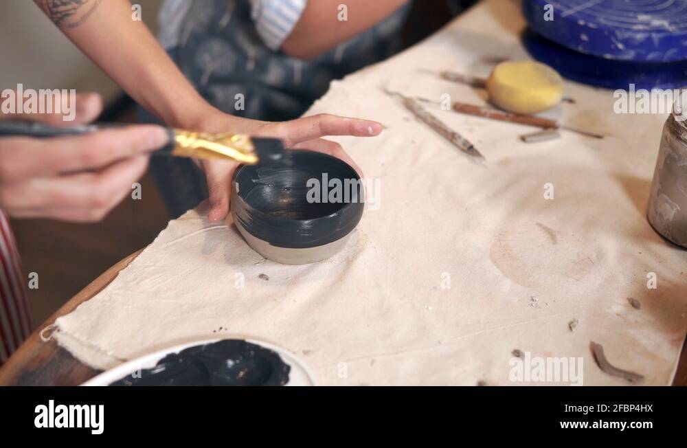 Female artist is coloring new clay cup by black dye in table of ...
