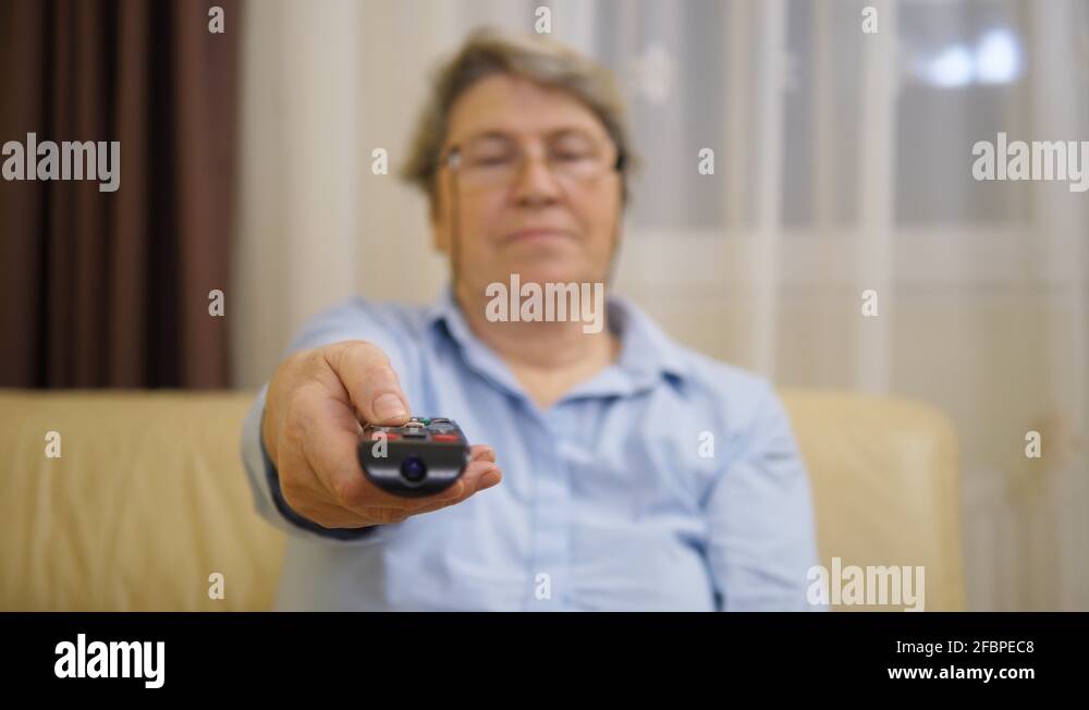 Detail of old woman hand holding remote control, grandmother face in ...