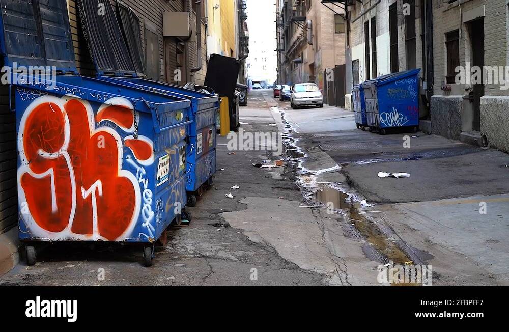 Alley way in a city with garbage on the street. Dumpster doors are ...