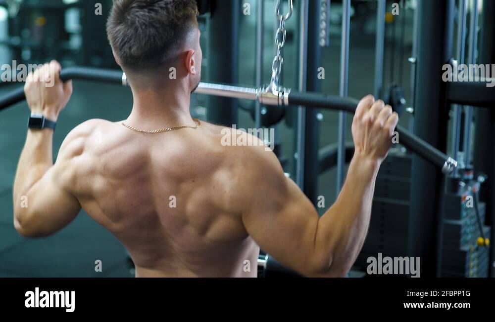Athlete trains in Gym, lifting blocks on rack machine, back view ...