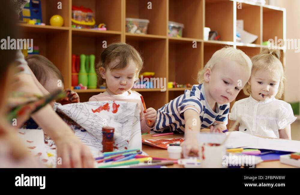 little children sit at the table and draw, kindergarten teachers remove ...
