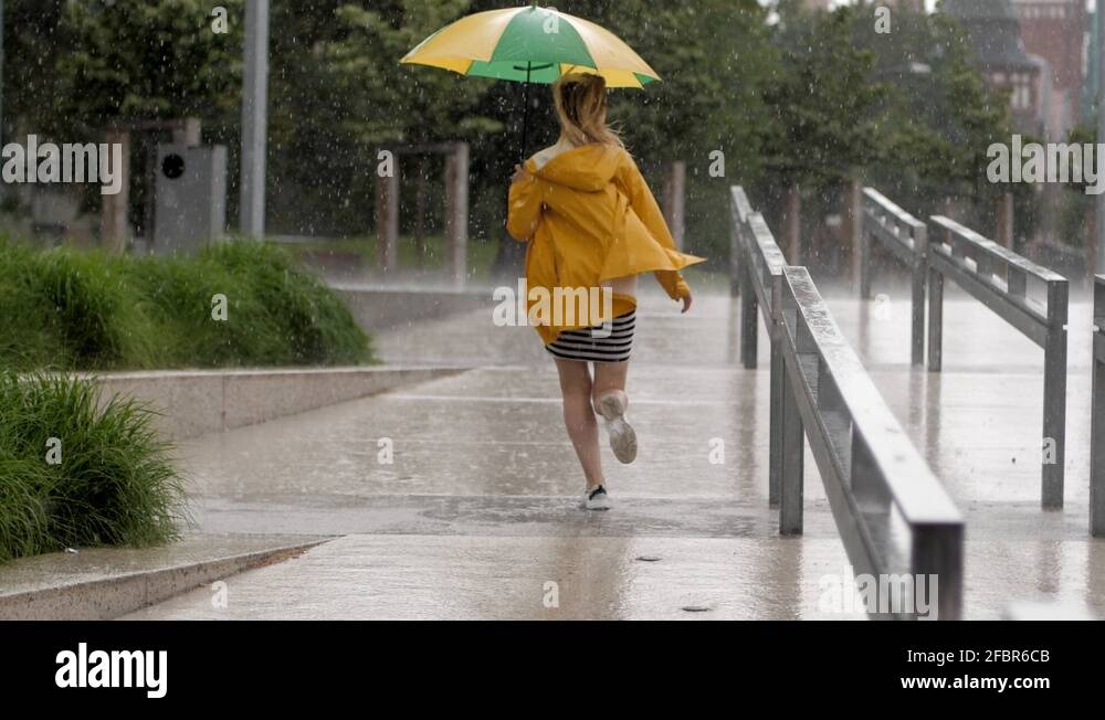Slow motion cute young girl run in shower rain with an umbrella wearing ...