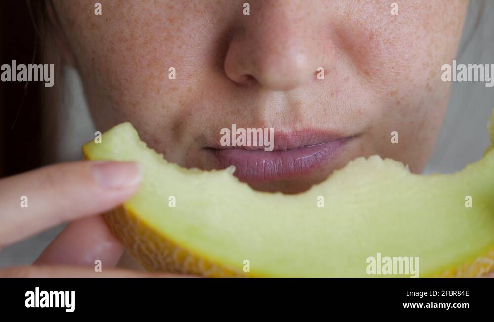 Woman with freckles on face is biting and chewing slice of melon, mouth ...