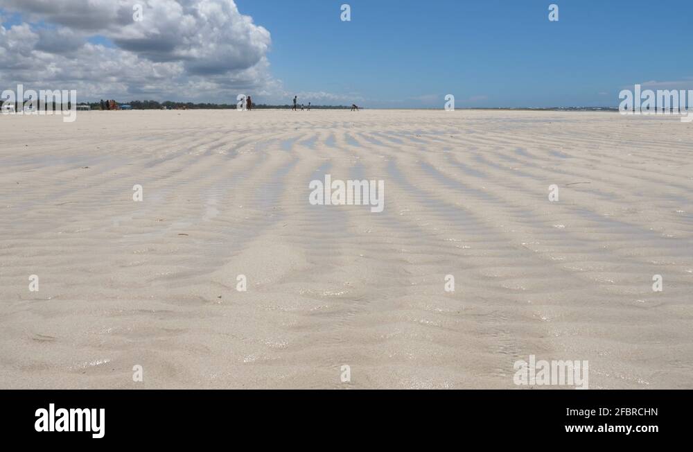 Static shot a wet, white sand beach, in Mombasa, people walking in the ...
