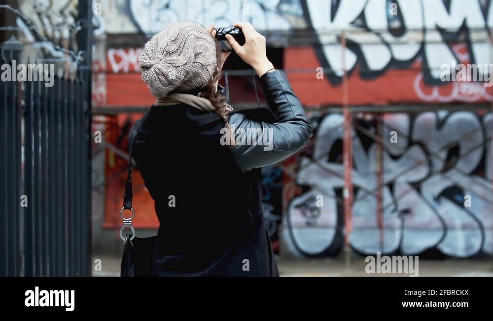 A woman taking pictures of graffiti on the buildings' walls with a ...