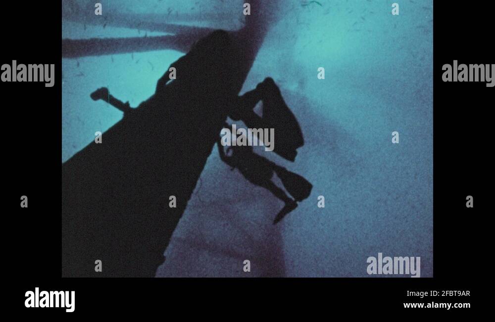 1970s: Men scuba dive in ocean, pop shells and barnacles off steel ...