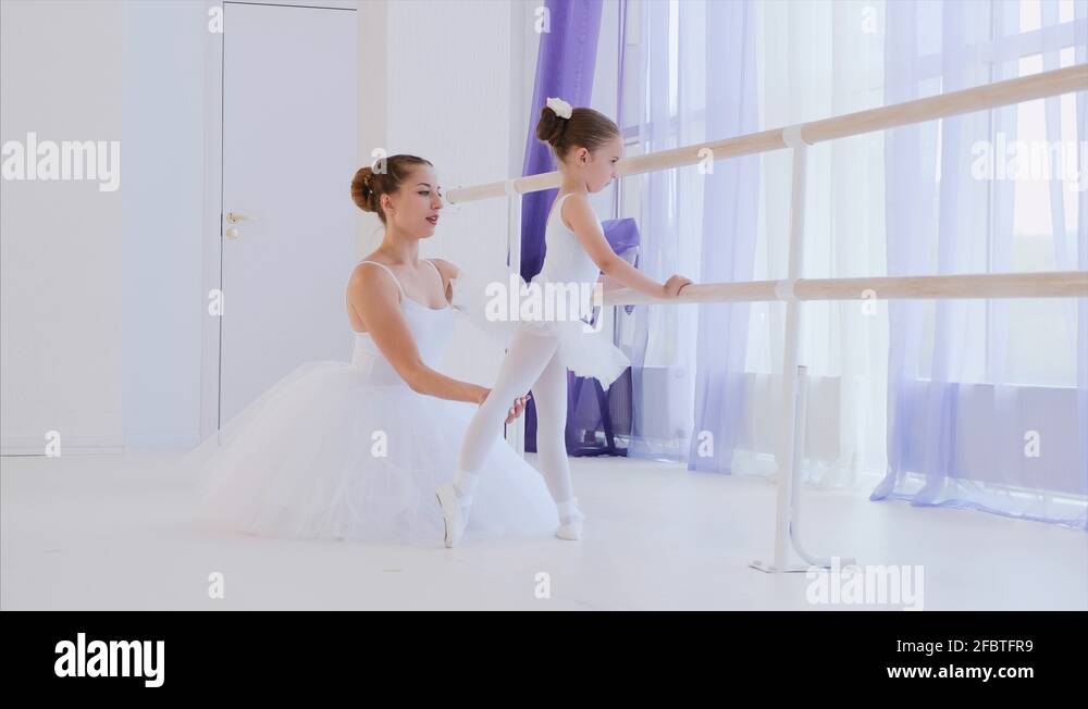 Ballet teacher is teaching little girl to stretch legs near the barre ...