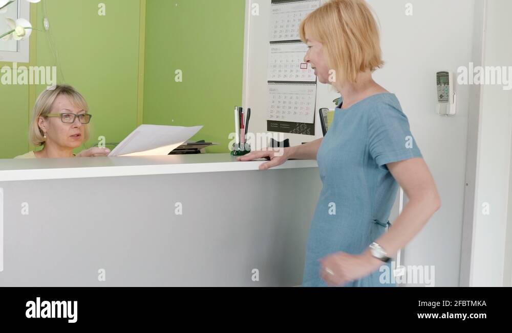 Woman patient with receptionist filling form at reception desk in ...