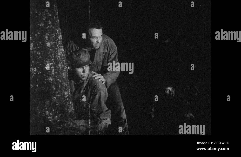 1950s: UNITED STATES: soldiers hide behind tree near road. Soldiers run ...