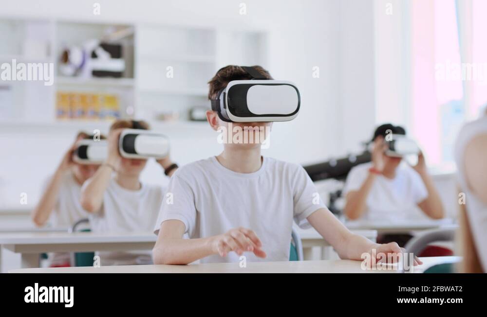 Preteen school children in white taking off VR headsets looking around ...