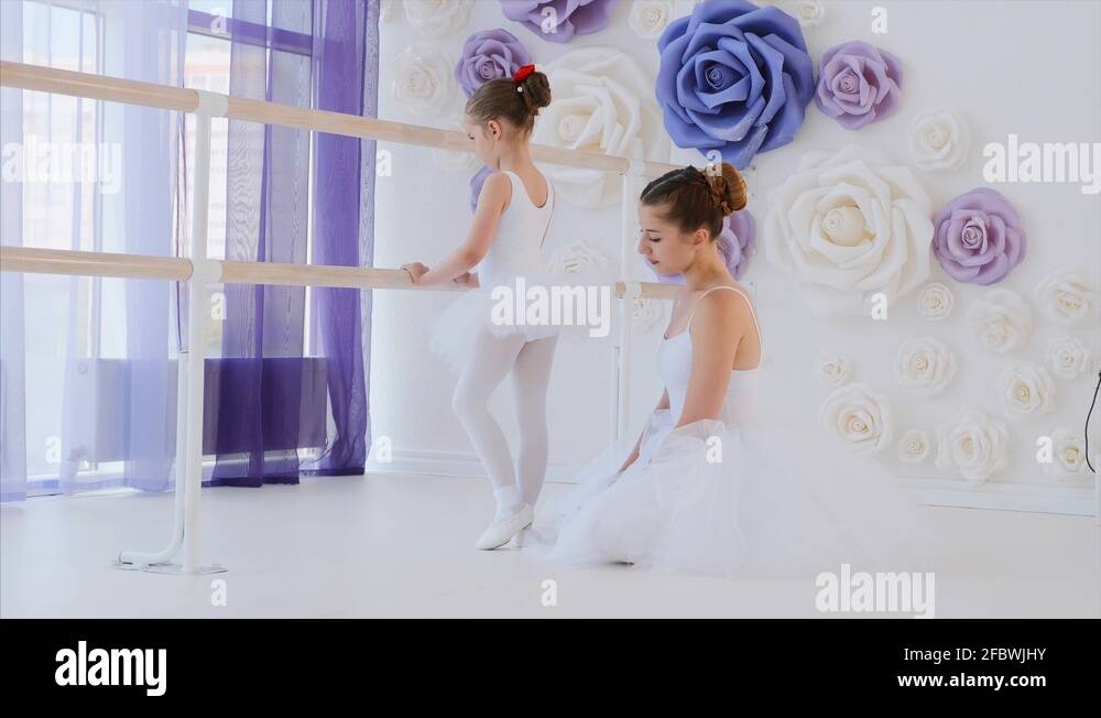 Ballet teacher is teaching little girl to stretch legs near the barre ...